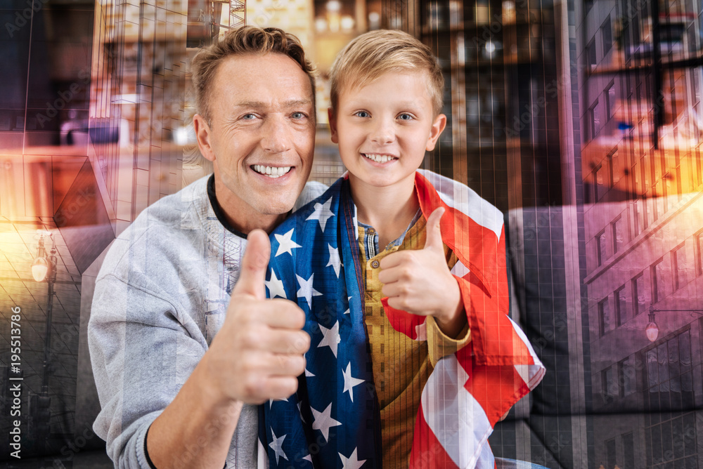 Looking happy. Positive friendly young man hugging his son sitting with ...