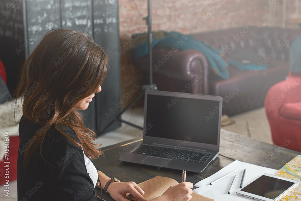 Profile of young female blogger with long dark hair working on open ...