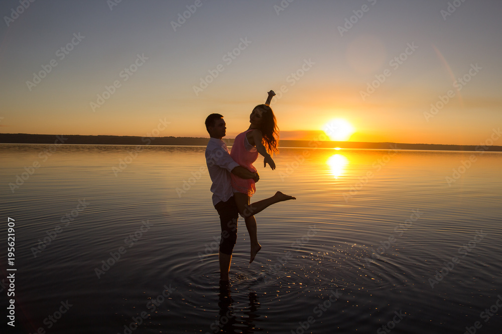 Young couple is dancing in the water on summer beach. Sunset over the ...