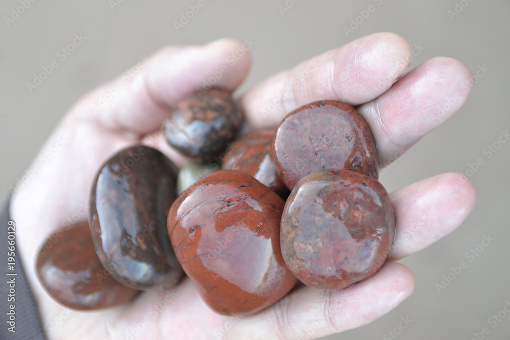 Sea pebbles in the palm of your hand. Man's hand holds red beach stones ...