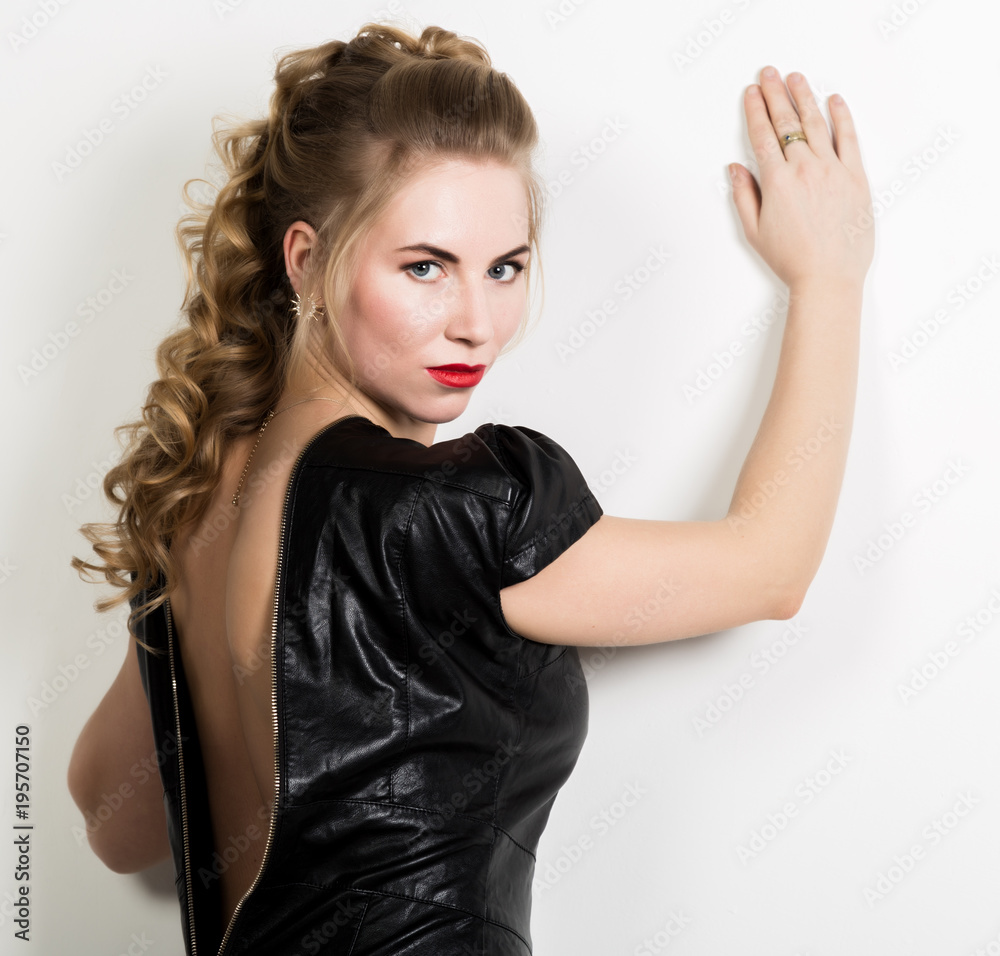 Beautiful young woman wearing short leather black dress with naked back on a light background ...