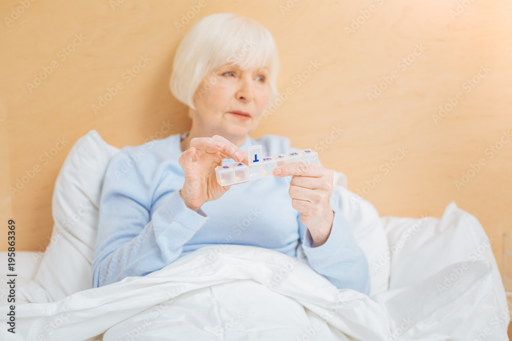Convenient pillbox. Tired ill senior woman feeling unwell and holding a ...