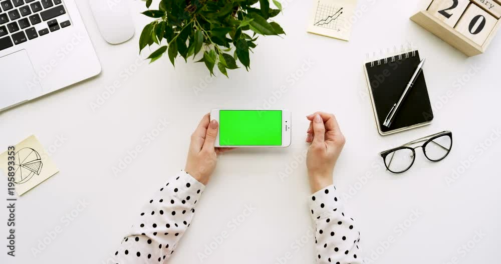 Top view on the office desk and white smartphone with green screen and ...