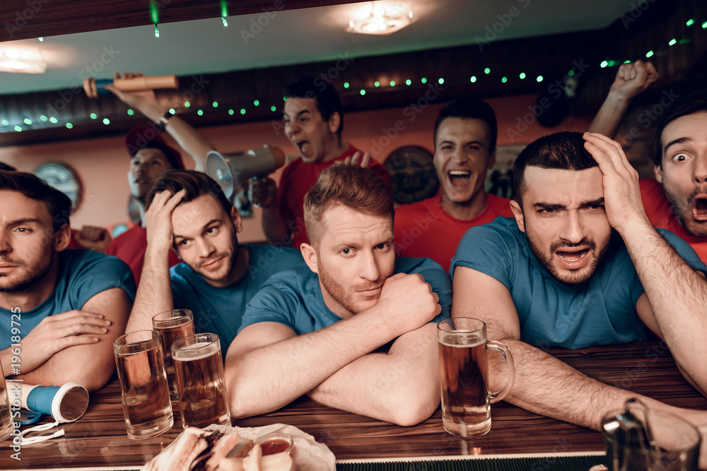 Sad blue team fans at bar in sports bar with red team fans celebrating ...