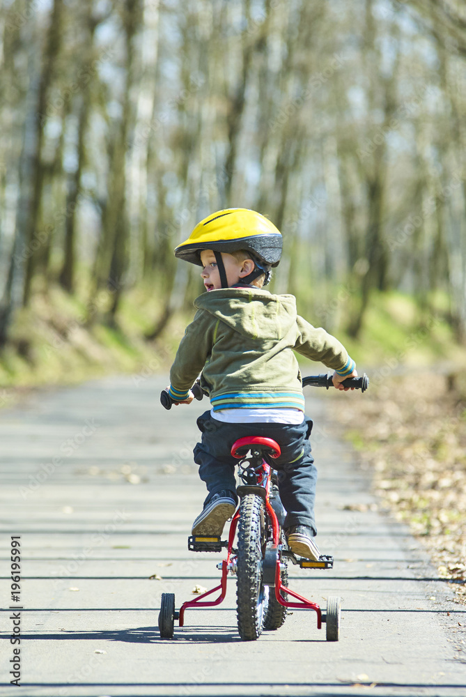 Little child boy cycling on bicycle in green park outdoor in spring. A ...