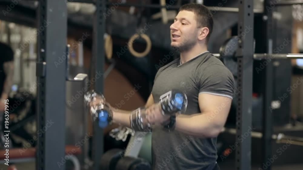 Strong man with an effort pumps his arm muscles with dumbbells. Brutal ...