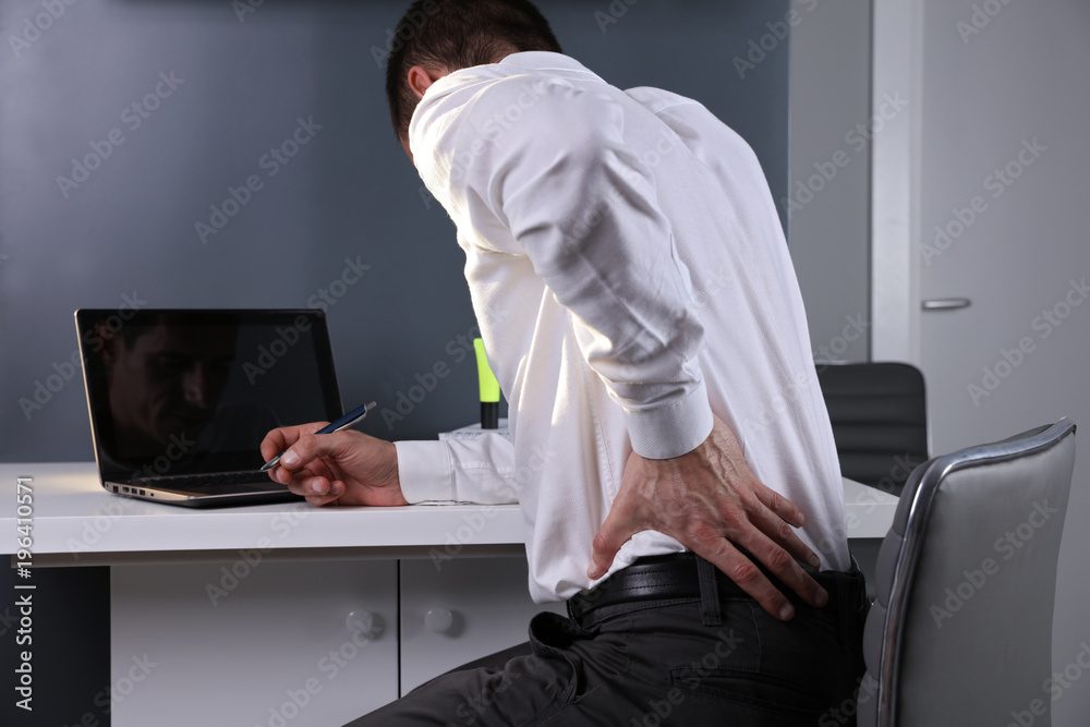 Business man suffering from back and neck pain in an office. Incorrect ...