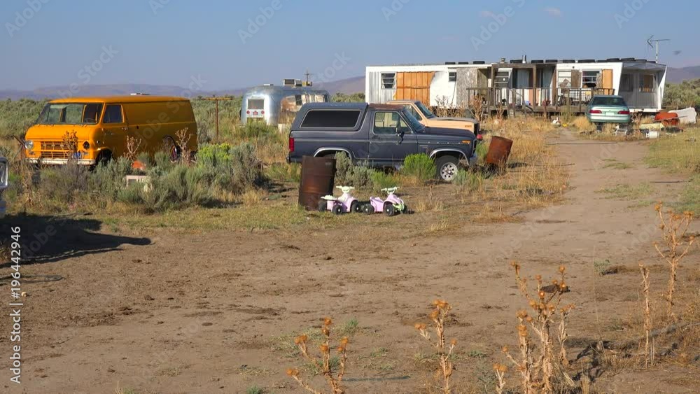 An abandoned mobile home in the desert is surrounded by old trucks and ...