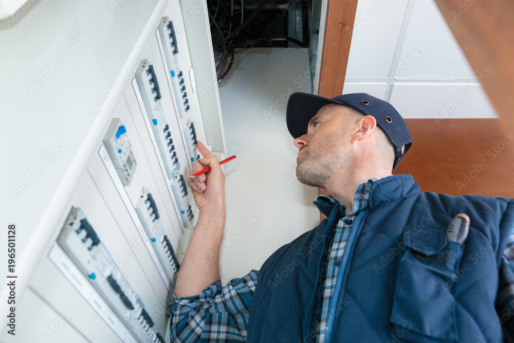 electrician working with electric scheme plan in front of fuse-switch ...