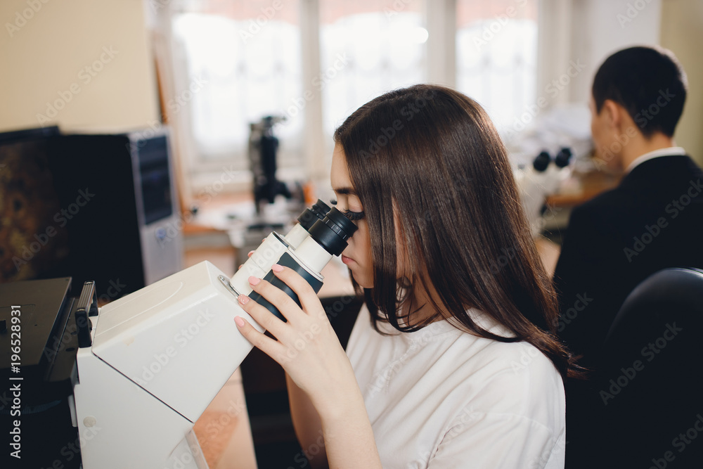 Student girl looks through a microscope in an equipped classroom with a ...