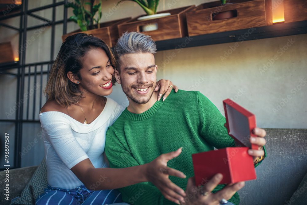 Happy interracial couple sitting in cafe bar. Man giving gift to his ...