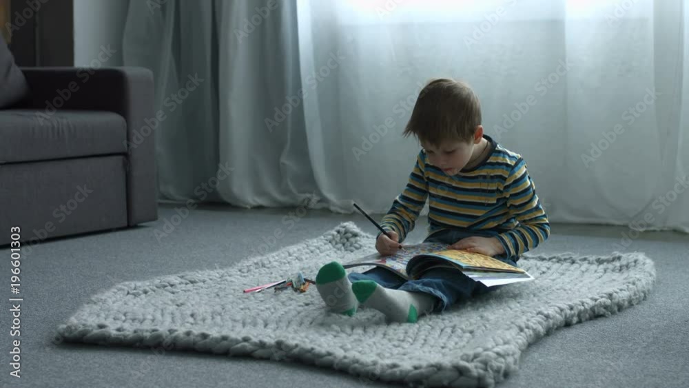 Concentrated preschool boy with pencil drawing in child maze book while ...