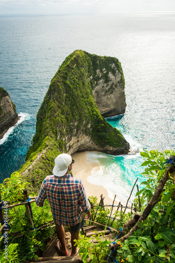 Man standing on a rock ladder at the edge of a cliff on Nusa Penida ...
