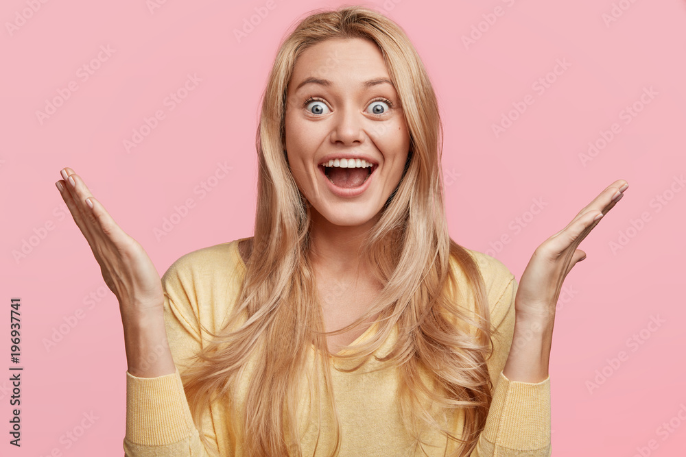 Emotional overjoyed female stares at camera, throws hands up, can`t ...