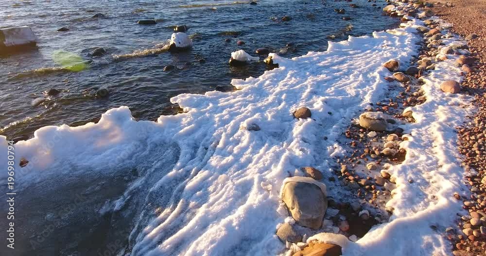AERIAL. Flying over an frozen sea coastline. Sunset reflections, snow ...