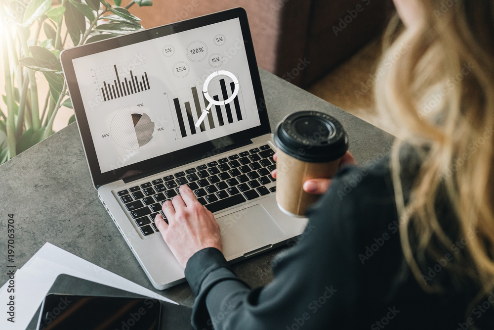 Rear view.Young businesswoman is standing near table,working on laptop ...