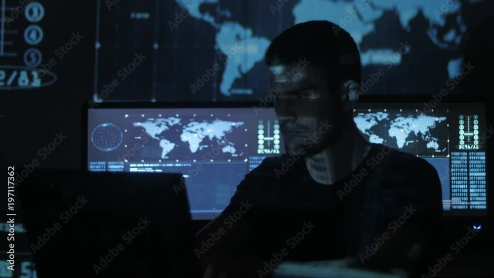 Male hacker programmer working at computer while blue code characters reflect on his face in ...