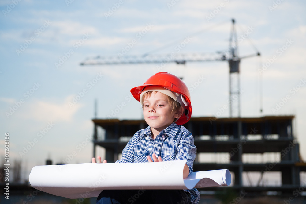 cute little boy in orange helmet sitting with paper project in hands on ...