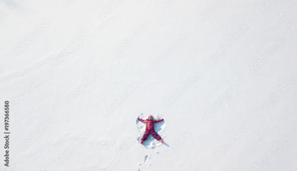 Child girl playing and making a snow angel in the snow. Top flat ...