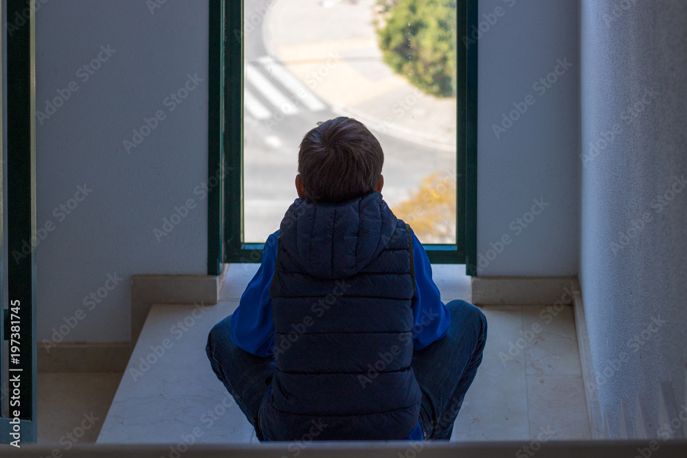 Sad boy sitting alone sitting in front of the window in the staircase ...