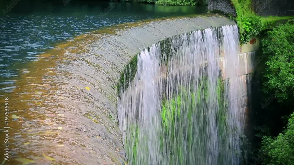 A wall of water flows from an old mossy historic disused water ...