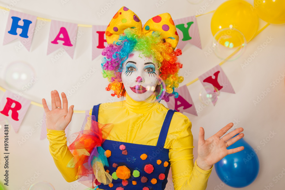A clown girl in a bright suit at the baby's birthday party. The ...