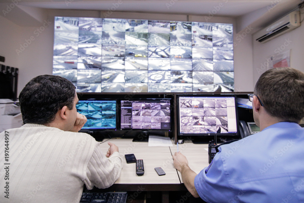 Two men observe display monitors with live images from road traffic in ...