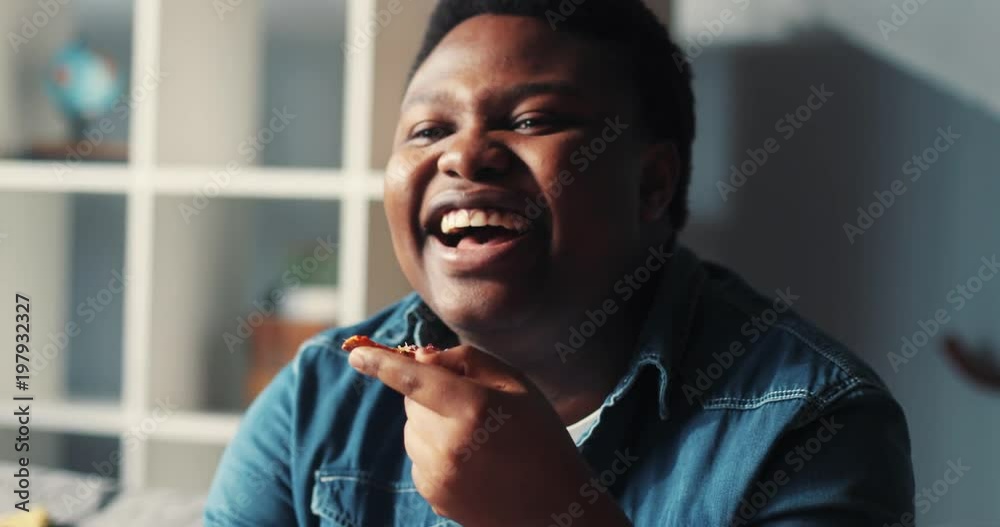 Close up face happy rude african american man watching tv sit on couch holds the remote smile ...