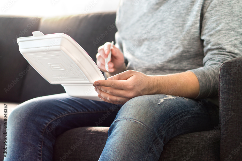 Man eating fast food from take away box home on couch. Takeout dinner ...