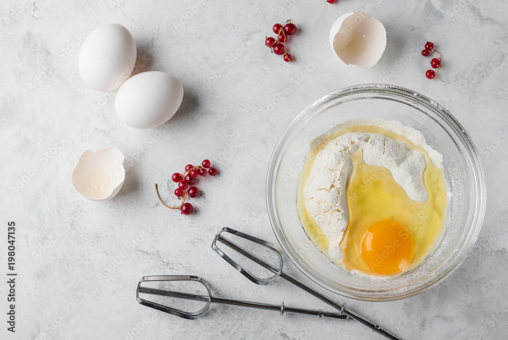 Top view photo of a broken egg on flour in a glass plate. Mixer fits on ...