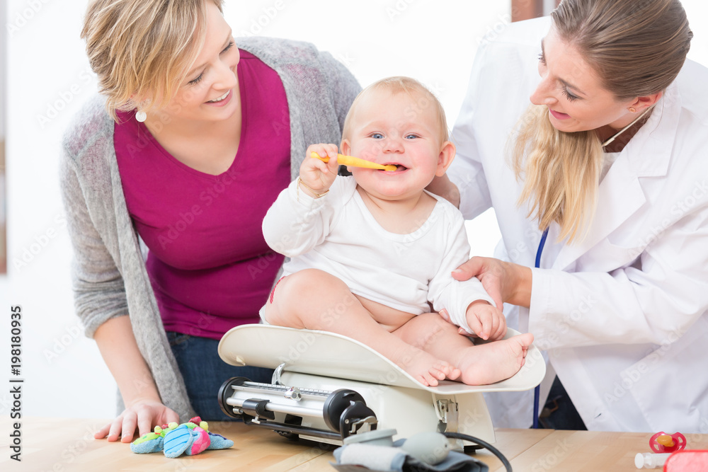 Female pediatric care specialist smiling while measuring the weight of ...