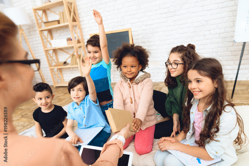 Group of children are pulling hands to answer teacher's question in ...