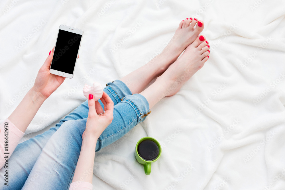 female feet, a girl uses a smart phone, blue jeans, red pedicure ...