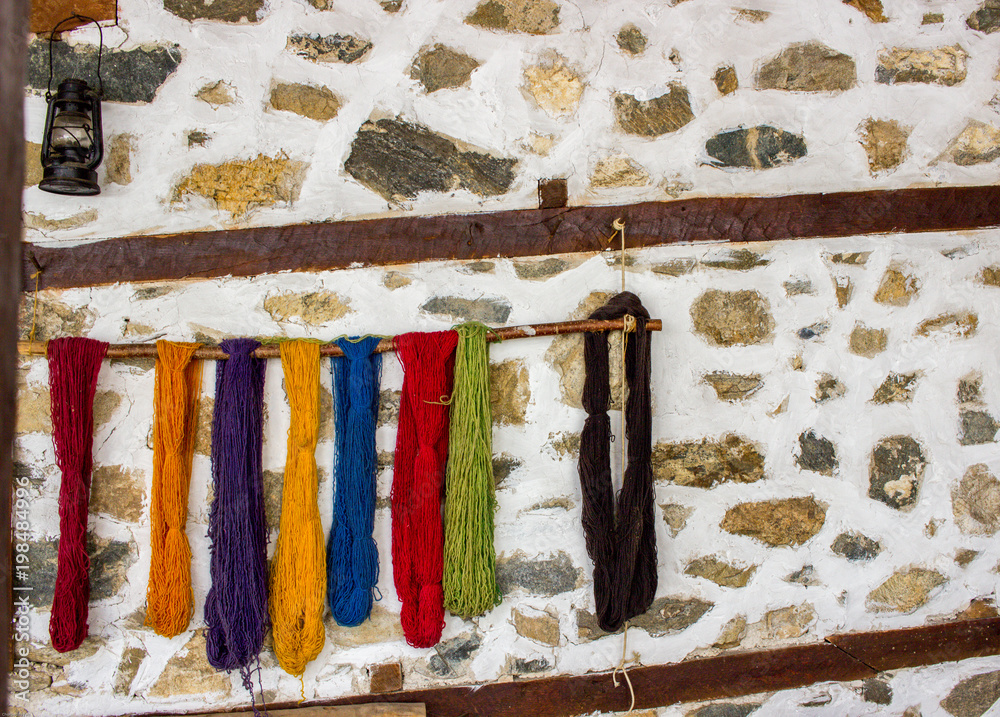Coloured woollen yam / yarn / tread hanging on stone and wood wall in ...