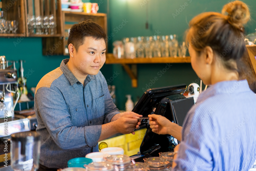 Friendly cafe cashier accepting payment from customer and taking credit ...