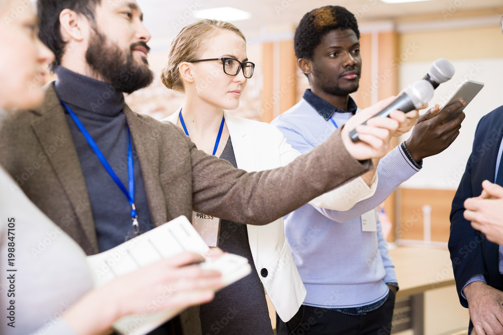 Multi-ethnic group of journalists stretching smartphones and ...
