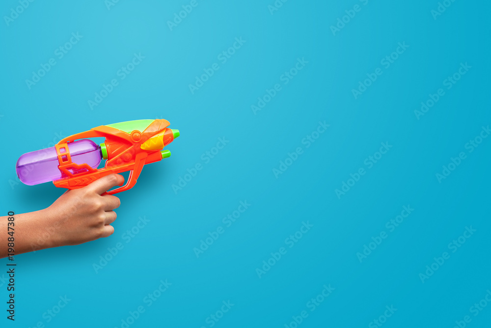 Hand holding plastic water gun on blue background. Objects with ...