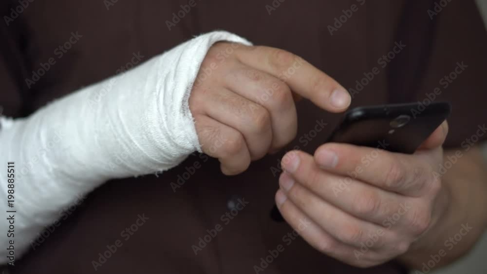A man with a broken right hand in a plaster uses a smartphone to search ...