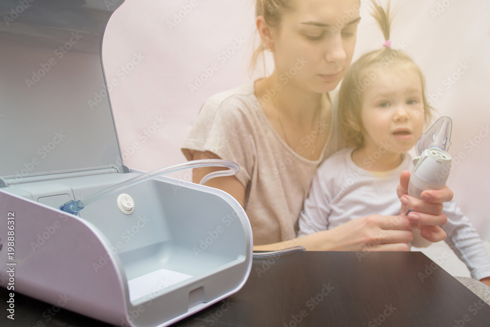 Two year old baby girl inhaling from the inhaler, her mother holding ...