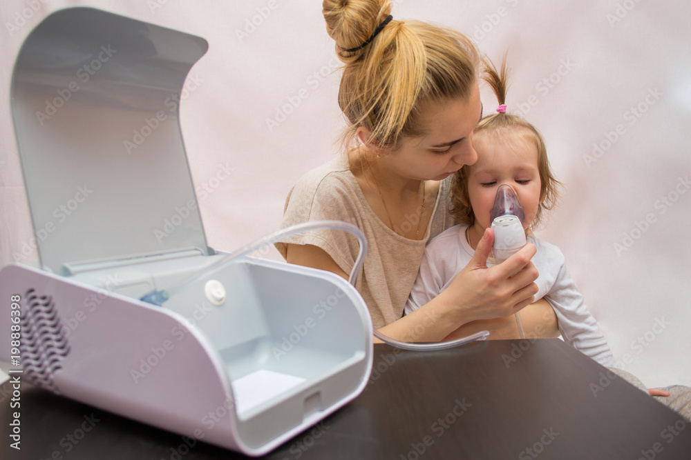 Two year old baby girl inhaling from the inhaler, her mother holding ...