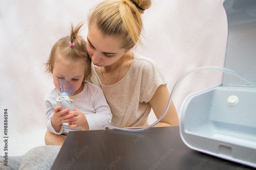 Two year old baby girl inhaling from the inhaler, her mother holding ...