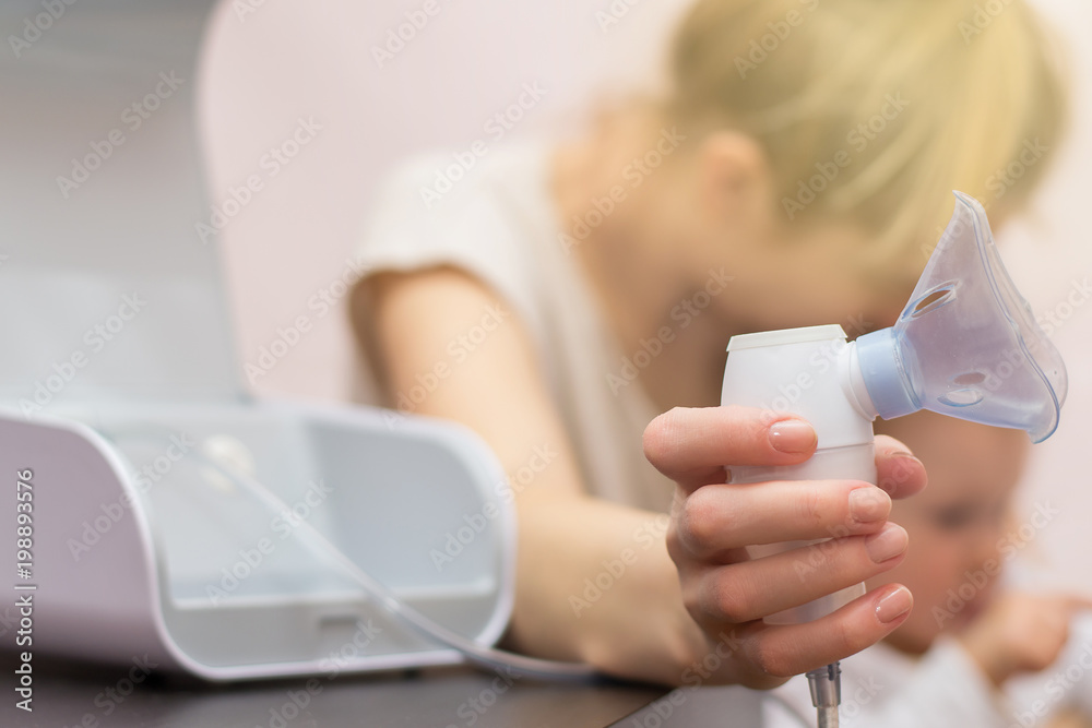 Two year old baby girl inhaling from the inhaler, her mother holding ...