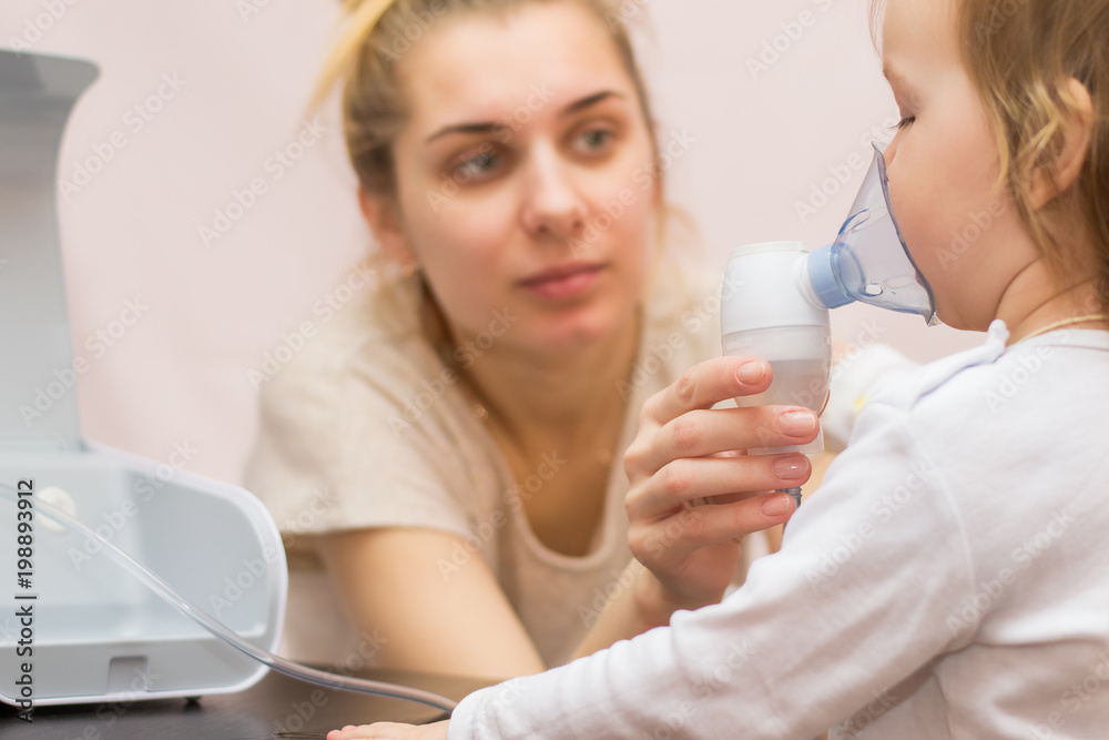 Two year old baby girl inhaling from the inhaler, her mother holding ...
