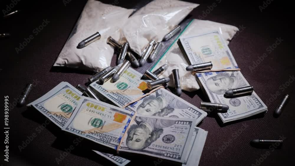 The gun and bullets fall down on the background of money and drugs ...