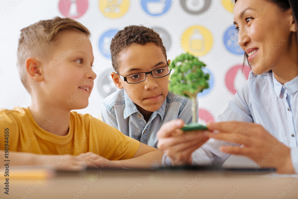 Best sample. Upbeat young teacher showing a tree model to her students ...