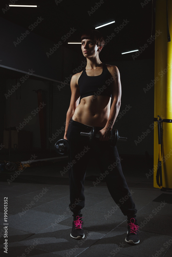 fitness girl doing exercises in gym with dumbels in dark hall, sporty ...