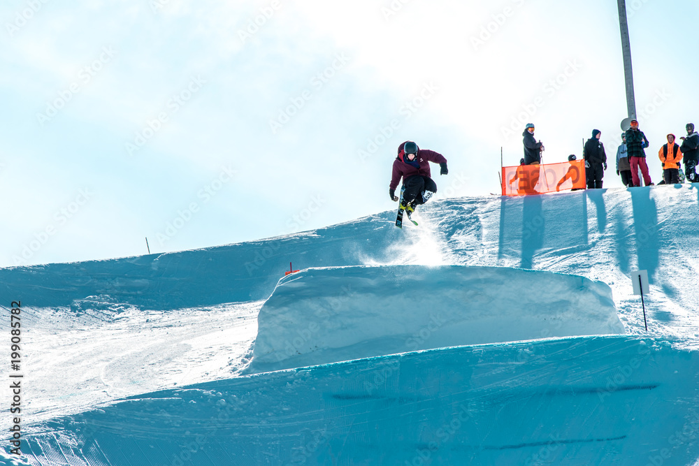 skier jumping off a ramp being watched by a small crowd as a little ...
