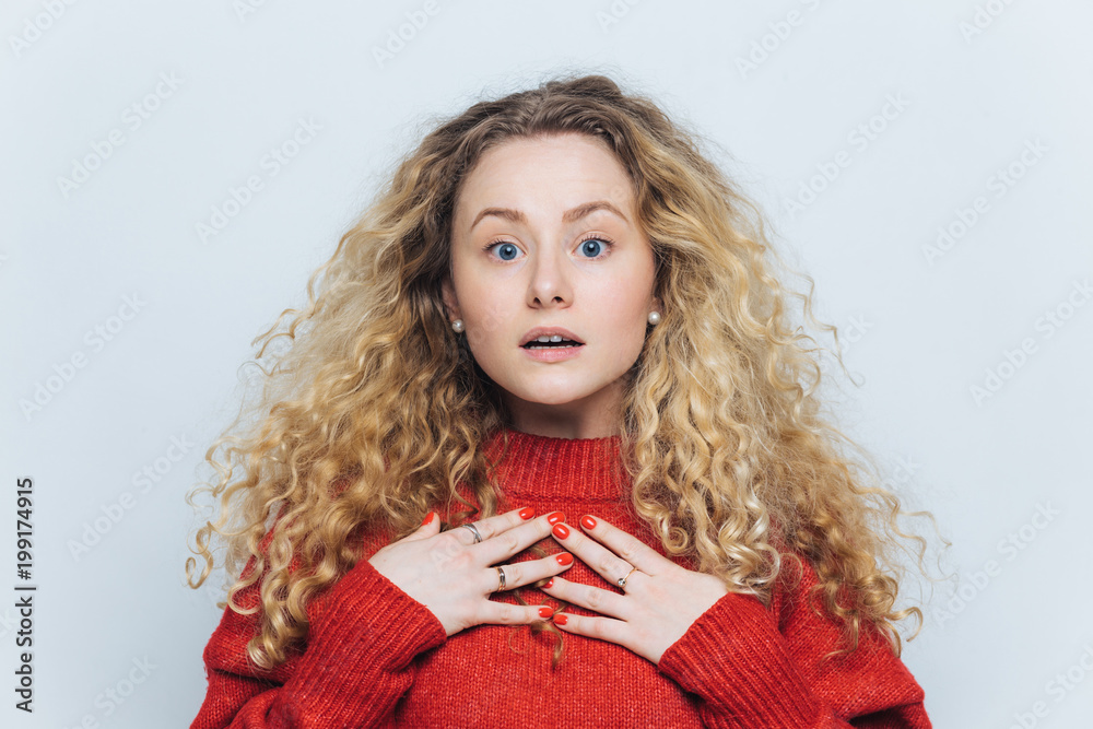 Stunned beautiful curly young woman looks with bated breath at camera ...