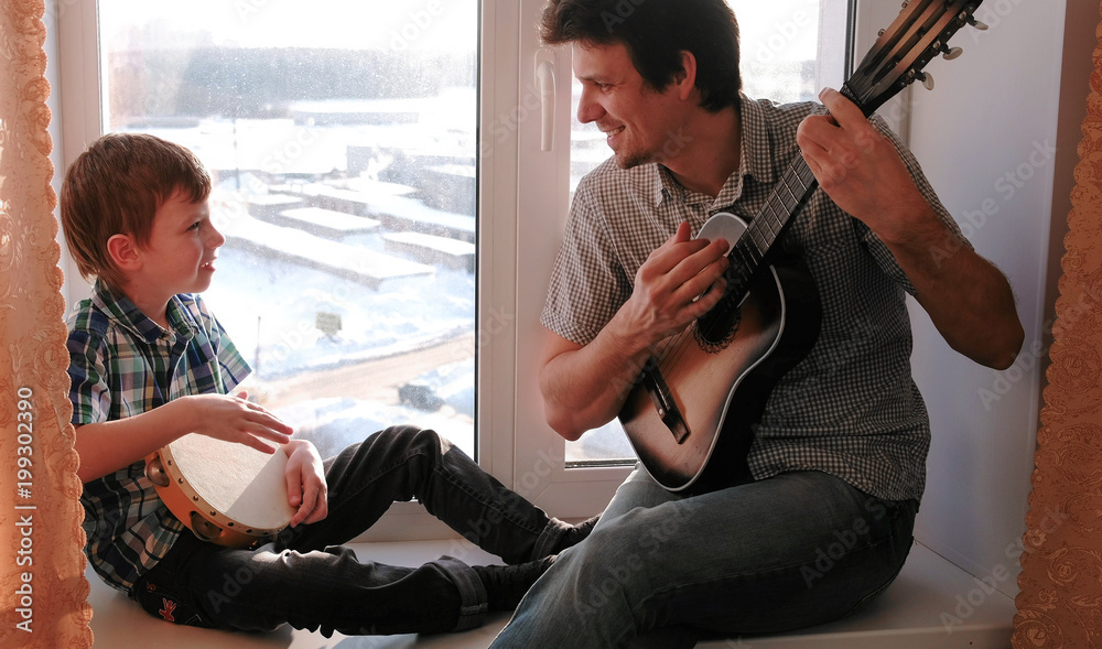 Playing a musical instrument. Dad is playing the guitar and son is ...