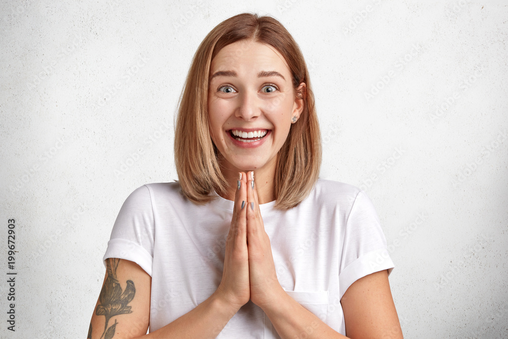 Happy pleased female keeps palms together, pleads about something her ...